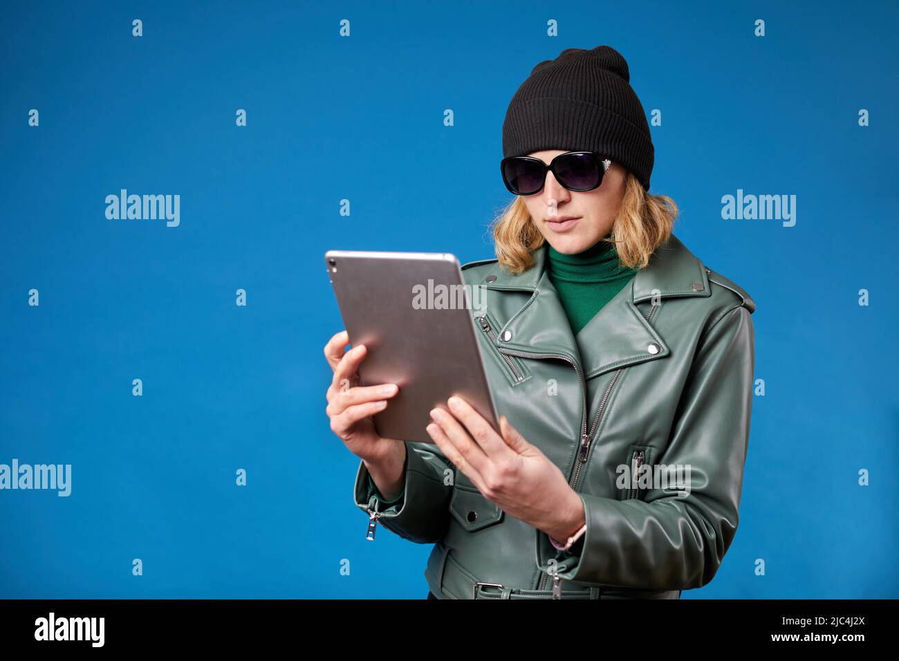 Side view of young woman using tablet computer isolated on a blue ...