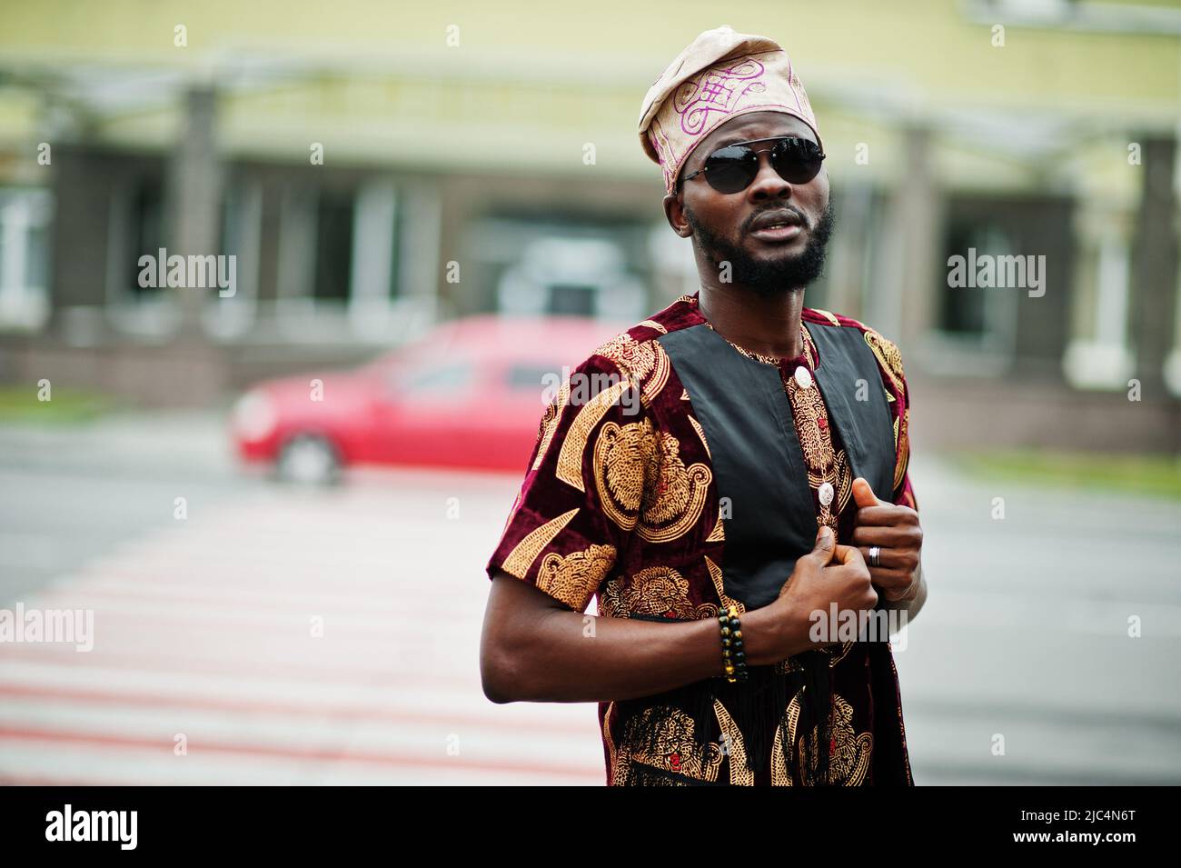 African stylish and handsome man in traditional outfit and cap standing ...