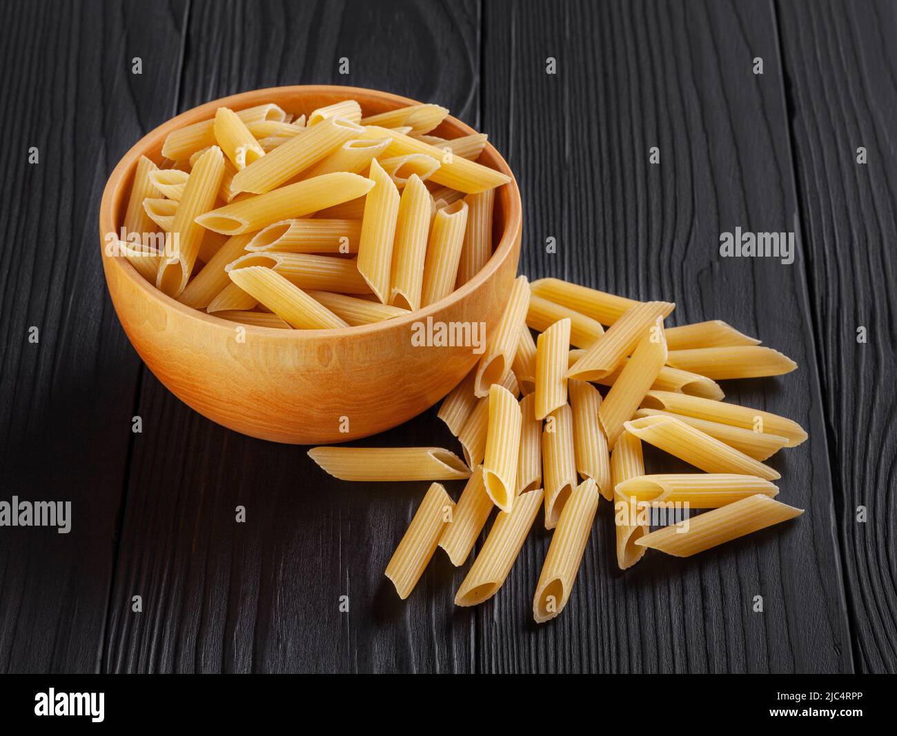 Uncooked penne pasta in wooden bowl on black wooden table Stock Photo ...