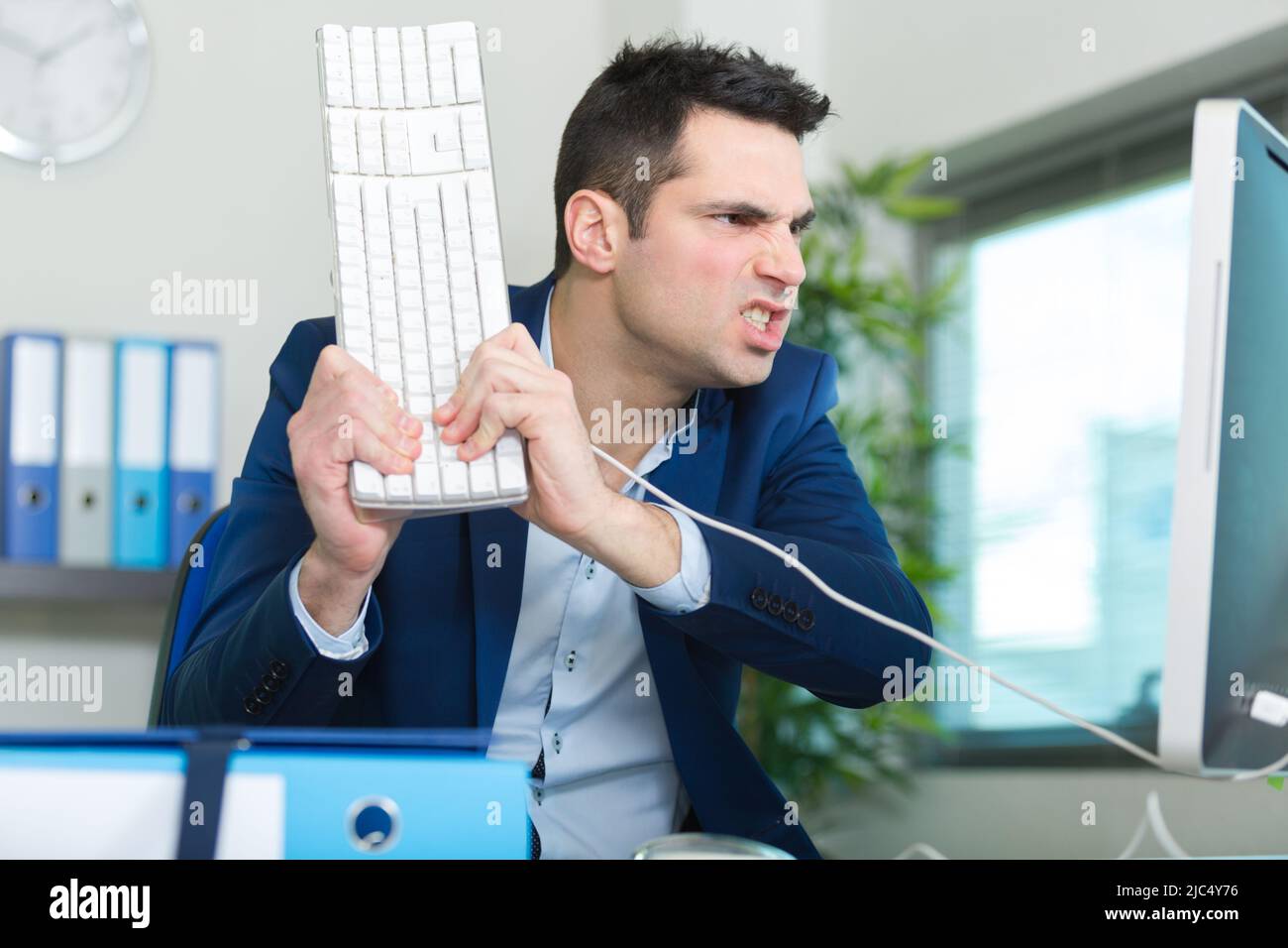 office worker trying to hit the screen with a keyboard Stock Photo - Alamy