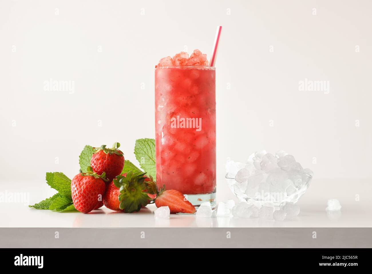 Strawberry slush drink in tall glass with fruit and crushed ice around ...