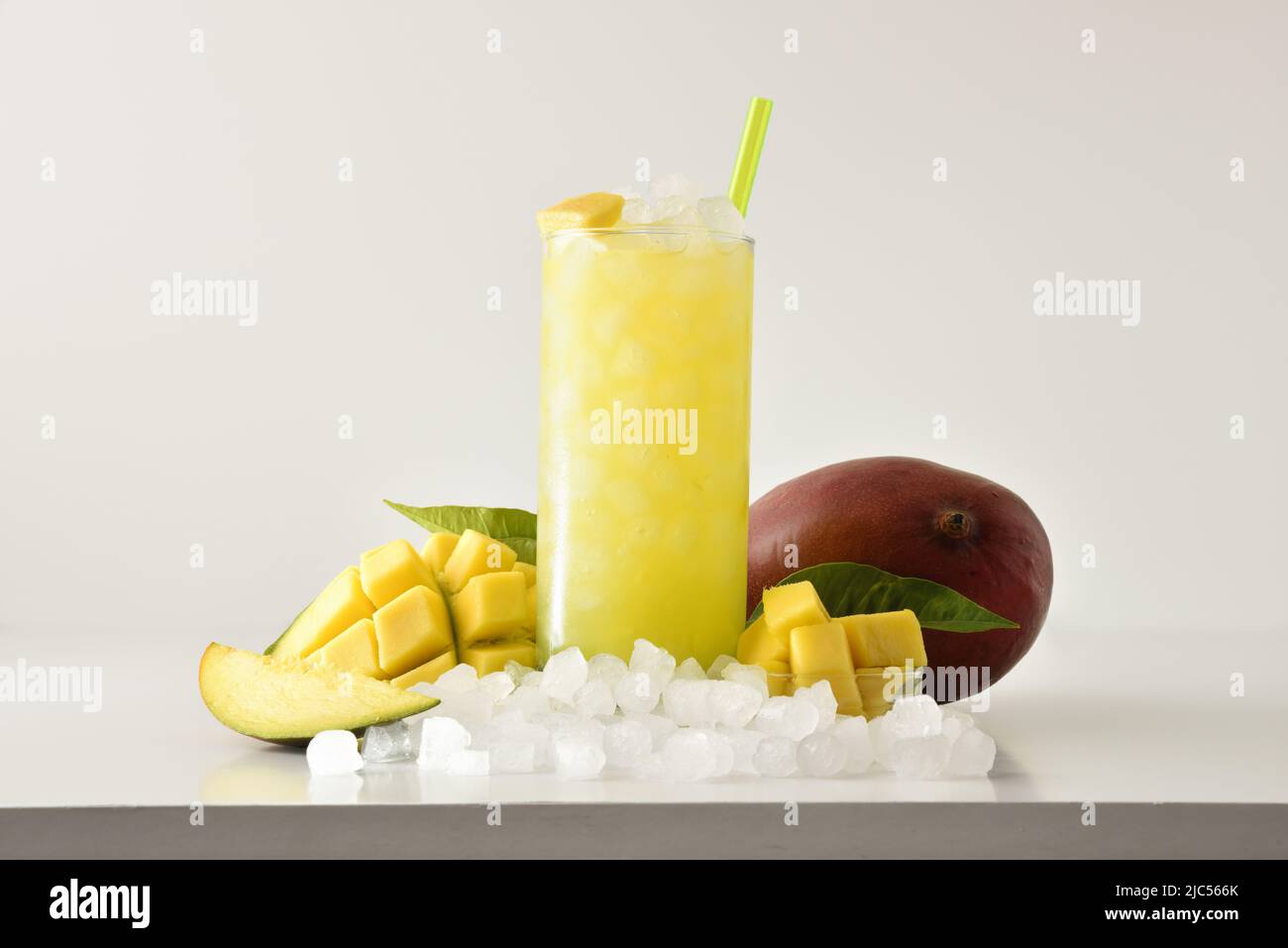 Mango slush drink in tall glass with fruit and crushed ice around it on ...