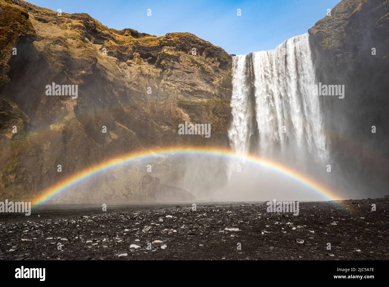 The mighty Skógafoss waterfall under a clear blue sky, with a beautiful ...