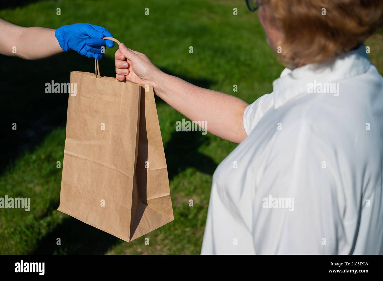 Female courier in gloves bringing food package to retired old woman ...