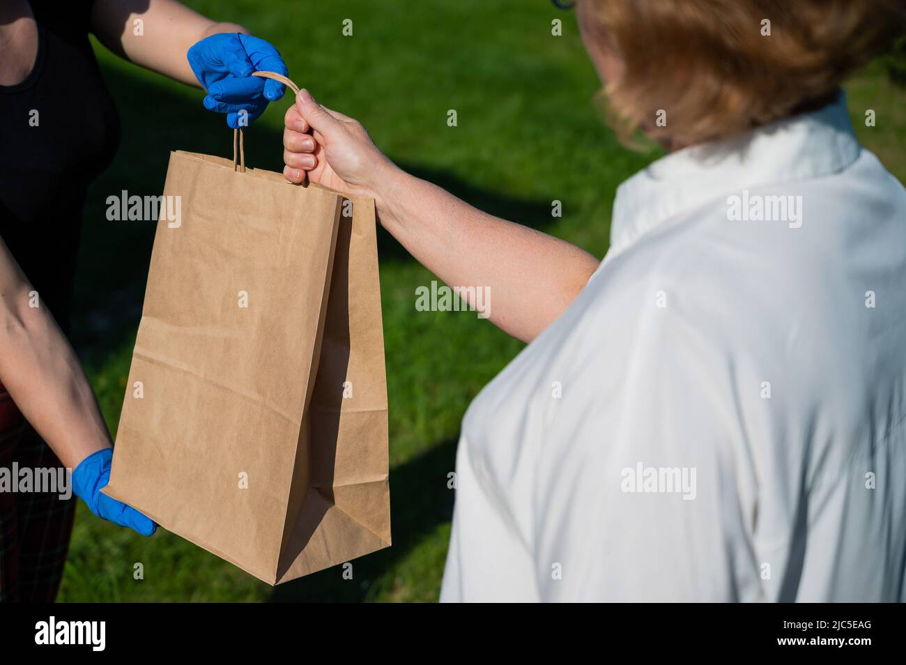 Female courier in gloves bringing food package to retired old woman ...