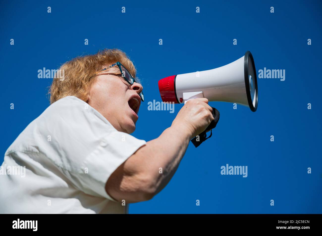 Emotional senior woman makes a speech in a megaphone on the outside. A ...
