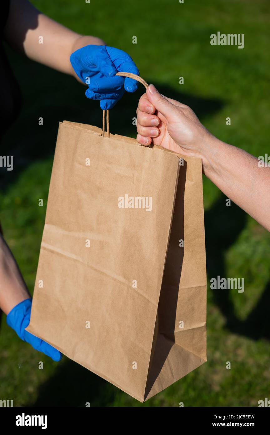 Faceless courier in gloves hands an eco friendly old lady's paper bag ...