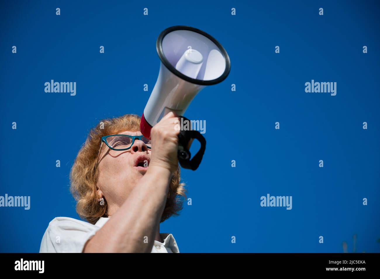 Emotional senior woman makes a speech in a megaphone on the outside. A ...