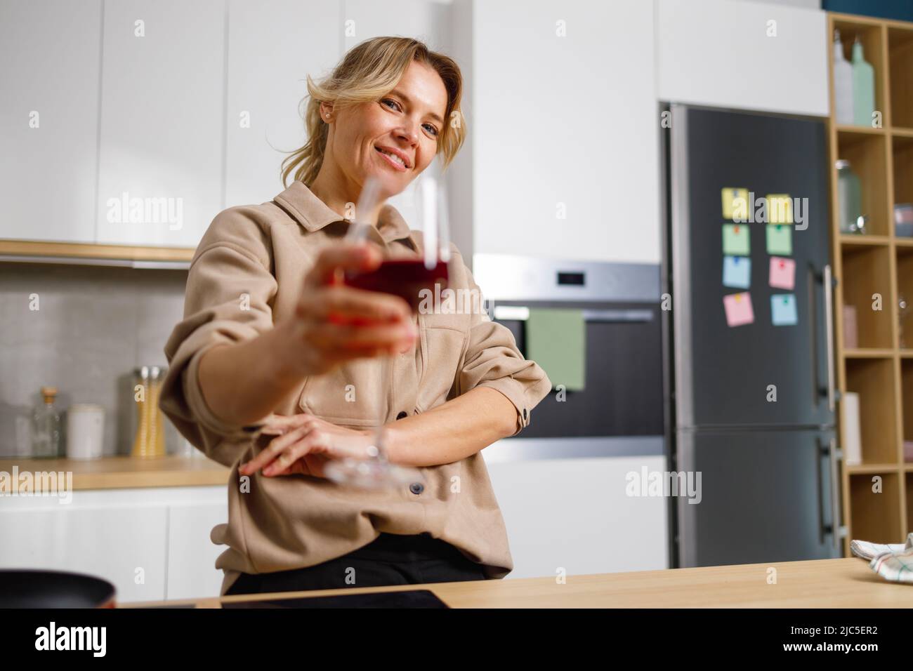Lonely woman with a glass of wine in the kitchen makes cheers. Female ...