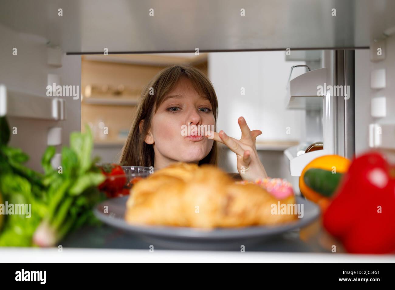 Girl opened the refrigerator and looks at the pastry food and tastes it ...