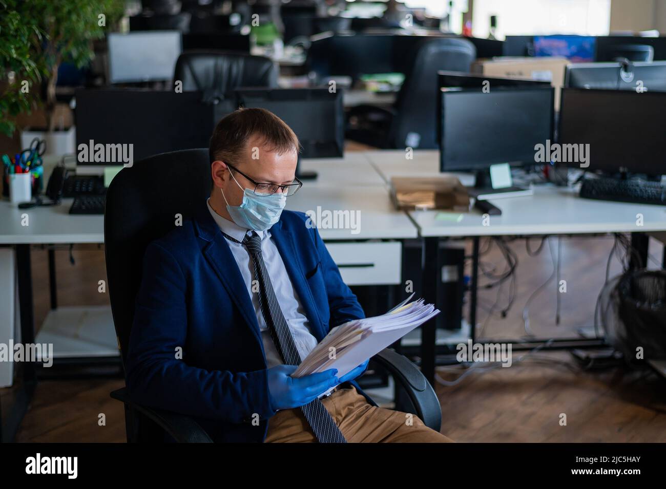 A man in a business suit and medical mask reads a paper report in an ...