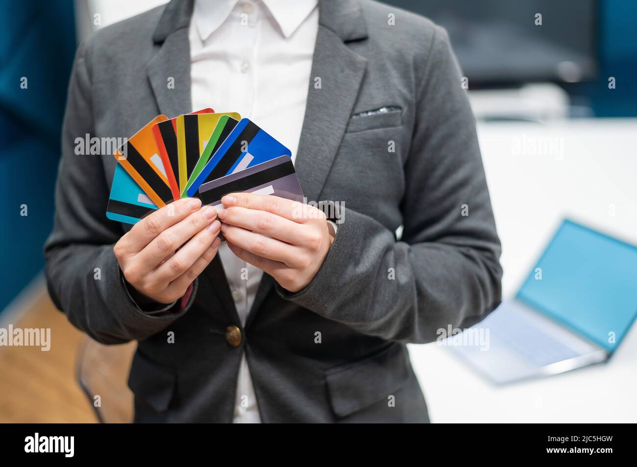 A faceless woman in a suit holds several multi-colored credit cards. A ...