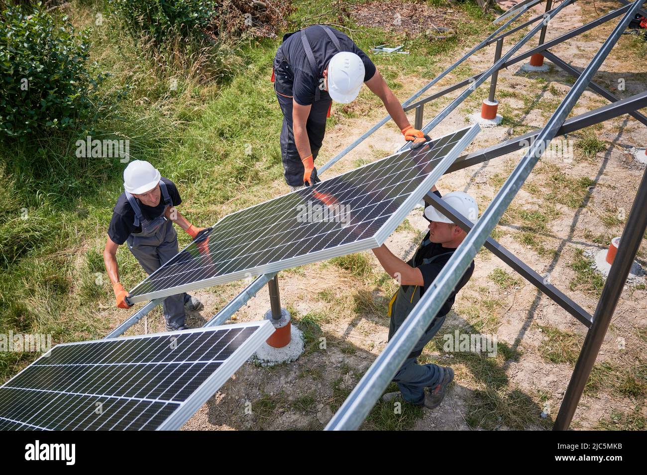 Workers installing solar panel on metal beams in field at sunny daytime ...