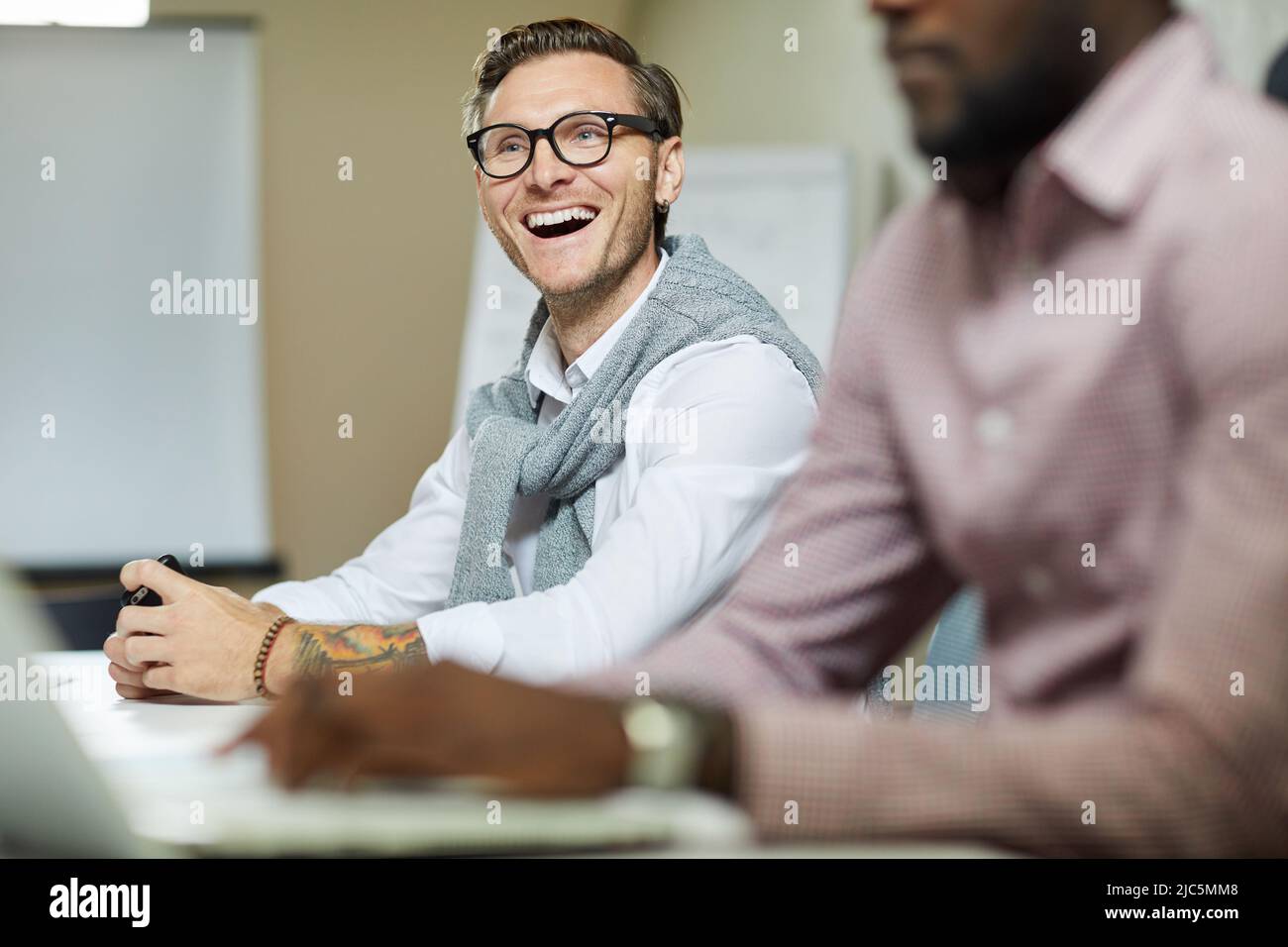 Ecstatic handsome young man with stubble sitting at table and laughing ...