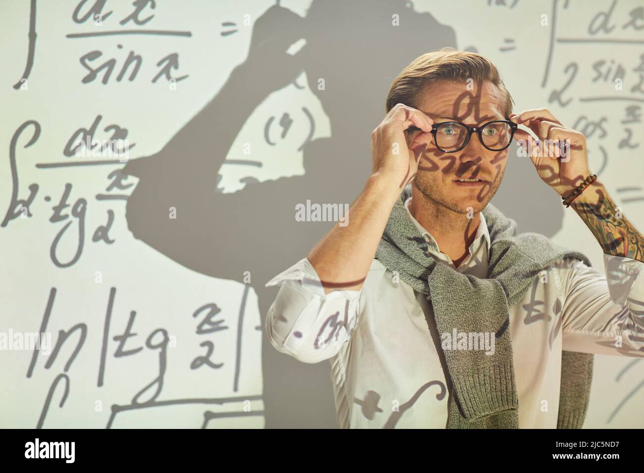 Serious pensive young math analyst with sweater around neck adjusting ...