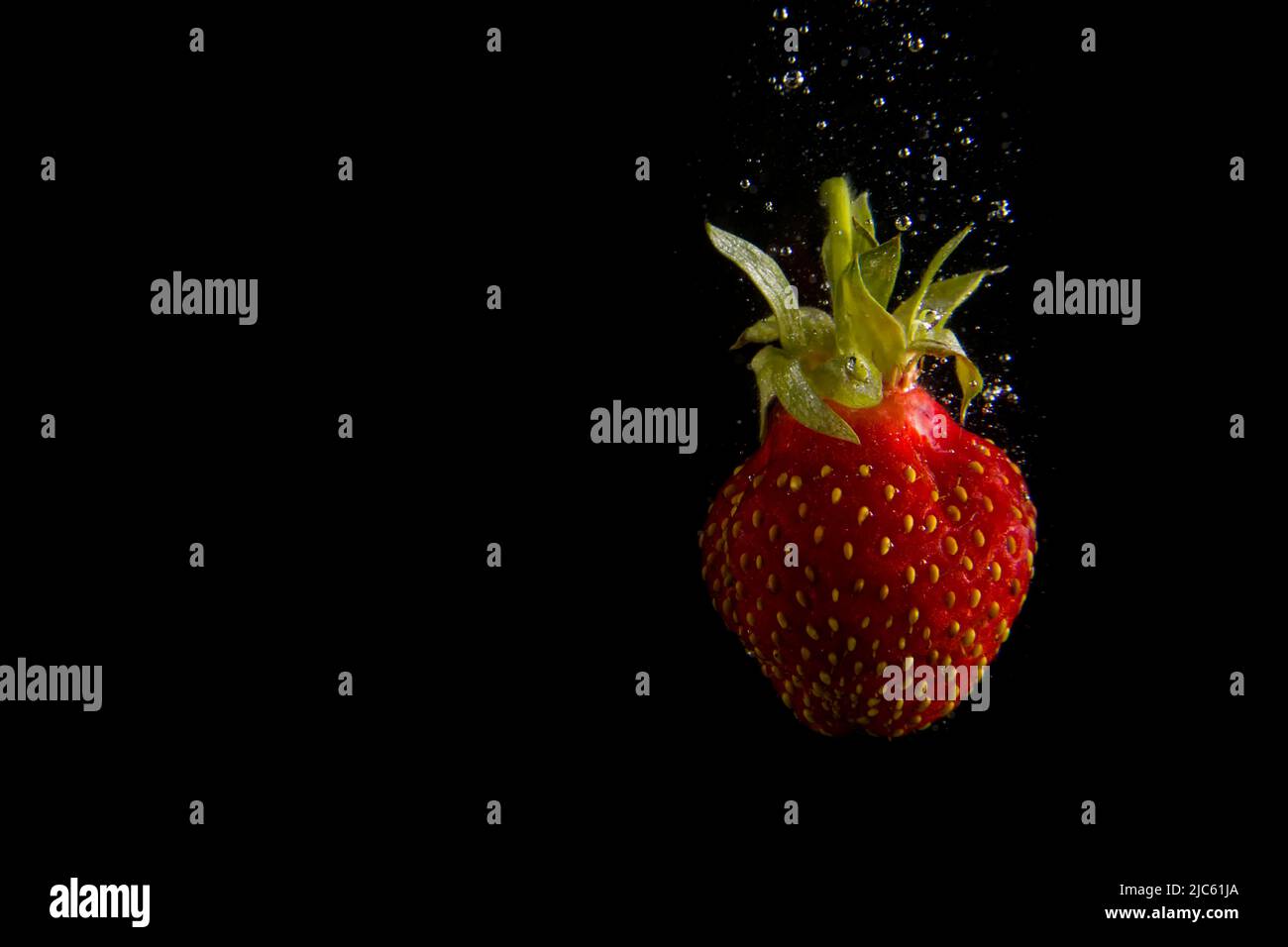 ripe strawberries fall into the water, raising splashes and air bubbles ...