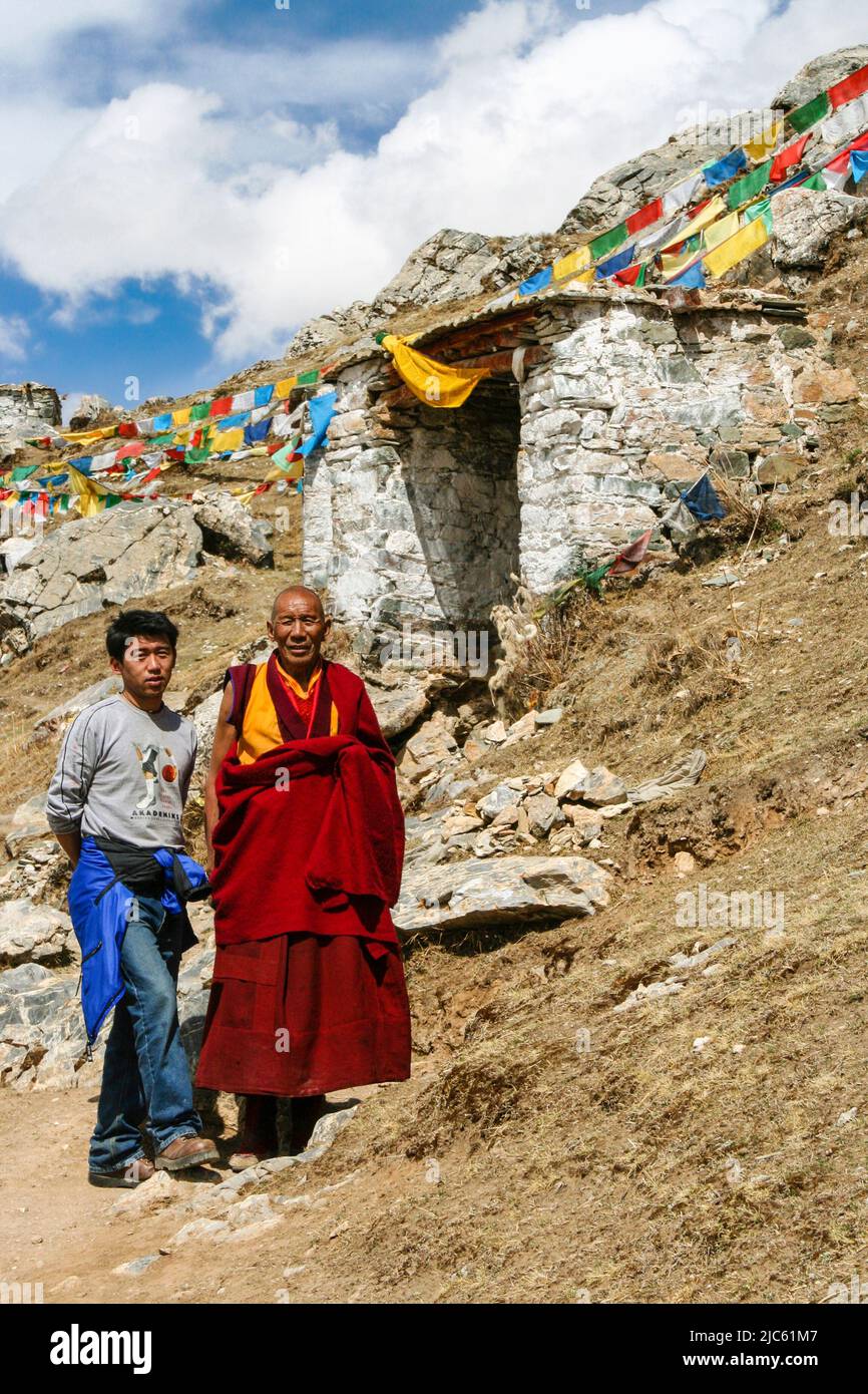 A Tibetan lama stands below prayer flags flapping in the wind along low ...