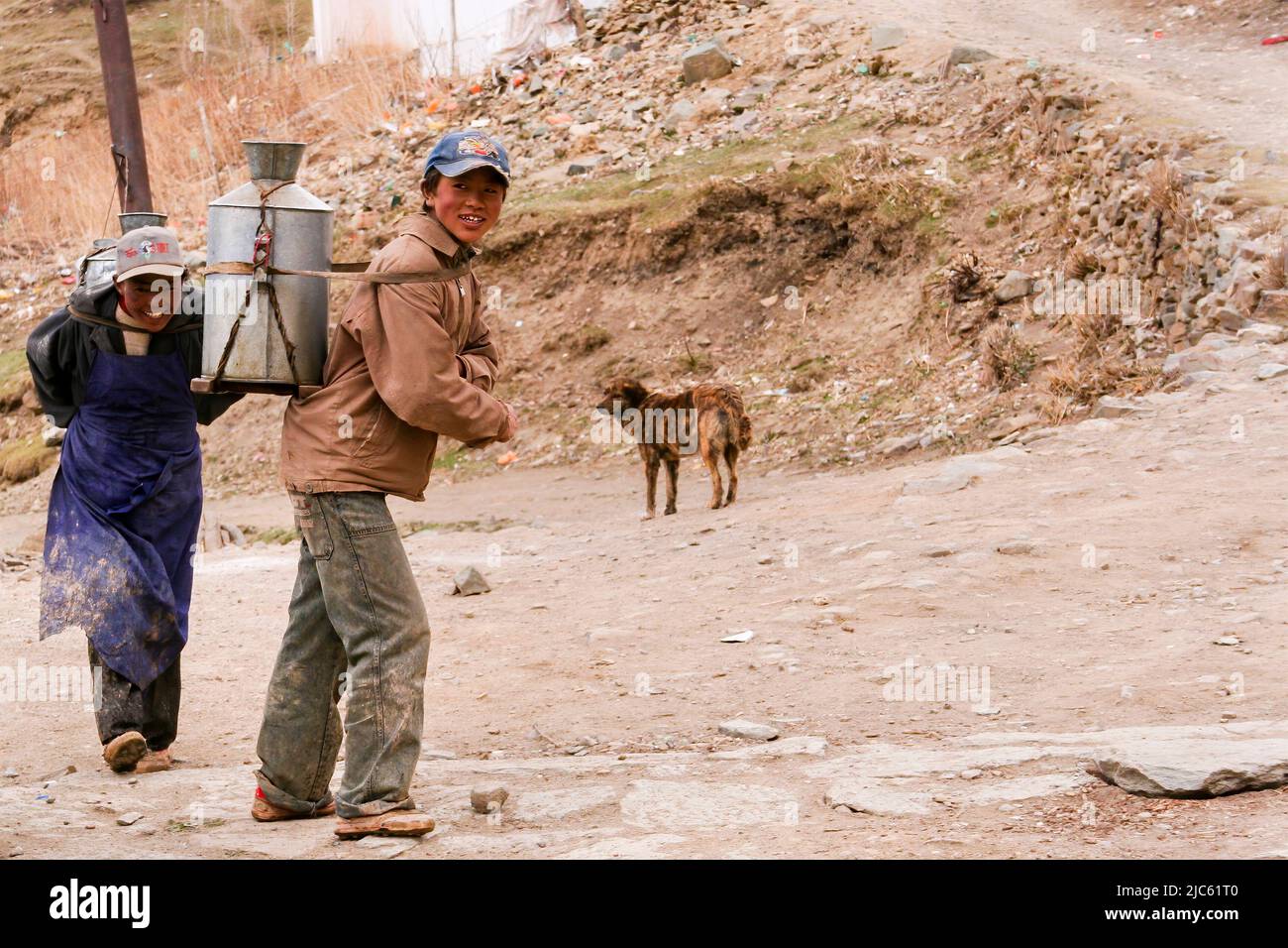 Two Tibetan youths carry milk in their milk jug at the Ganden Monastery ...