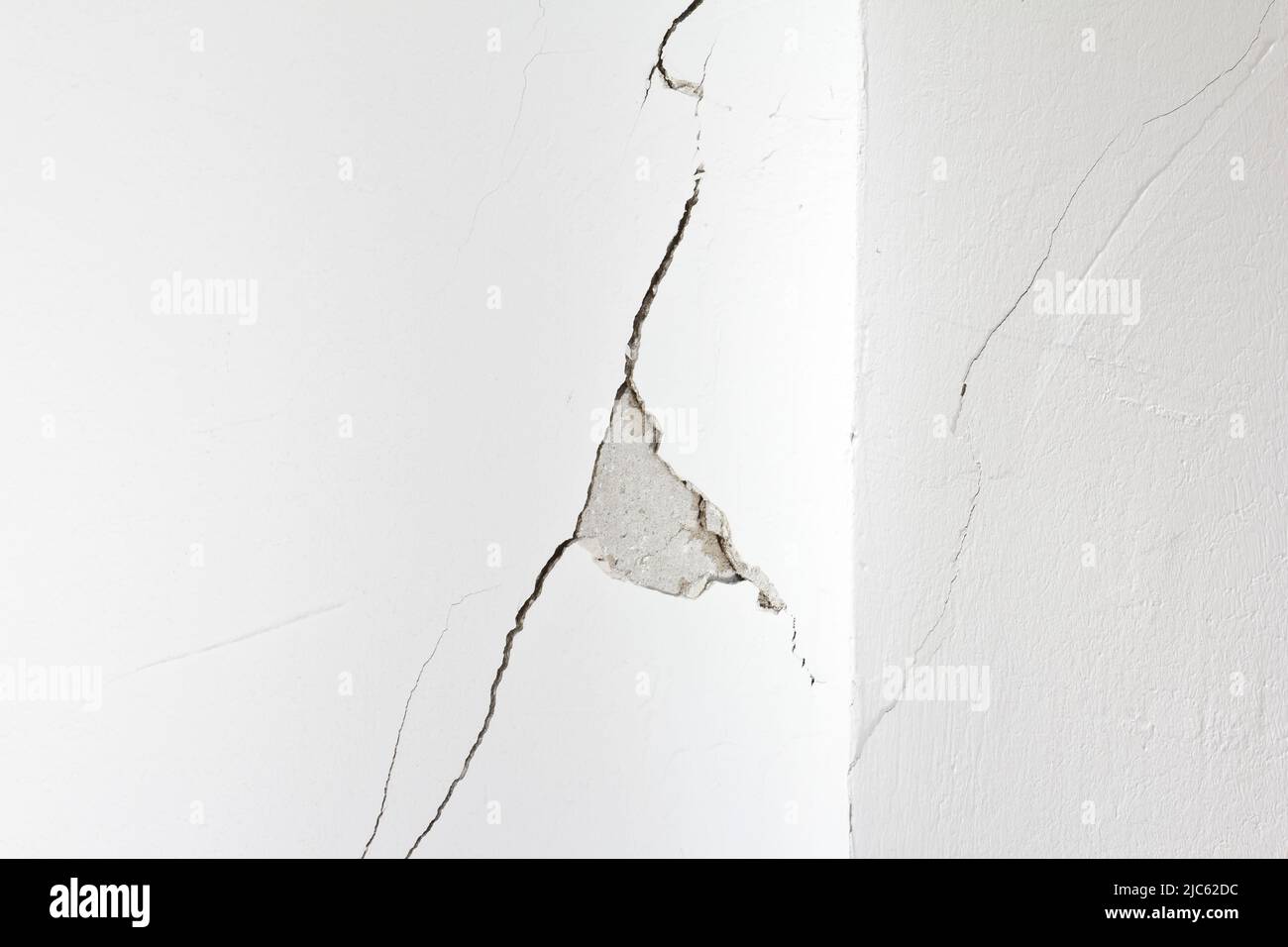 Damaged white wall with a long crack or rip and a piece of plaster ...