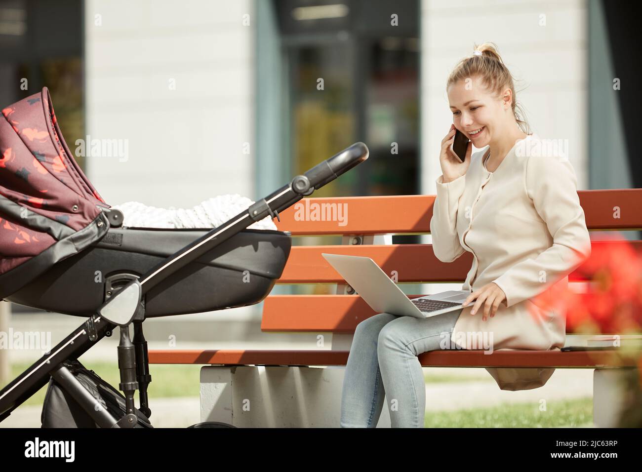 Young attractive mother working on her laptop and smartphone sitting ...