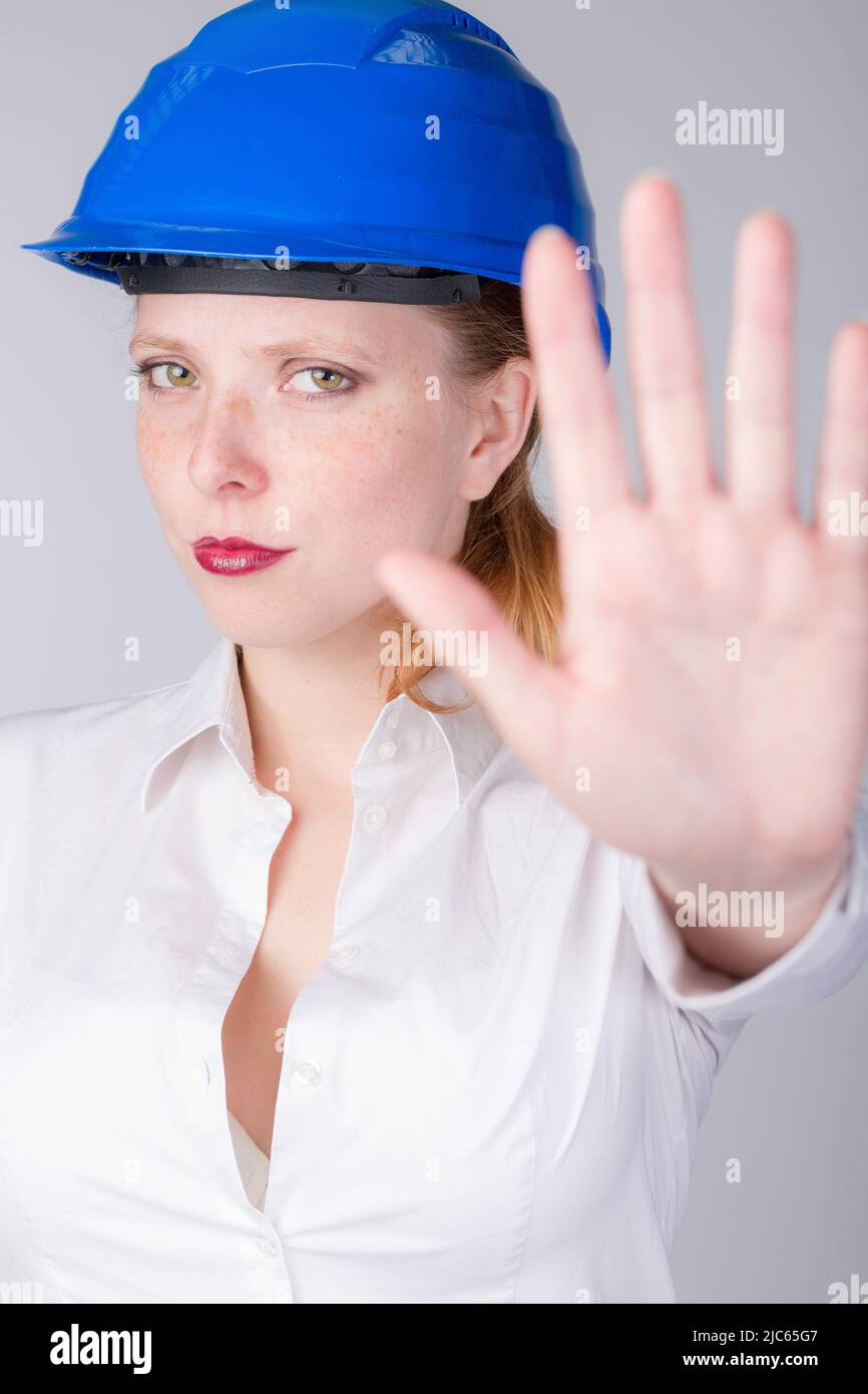 Young female engineer wearing a blue hard hat is making a stop gestures ...