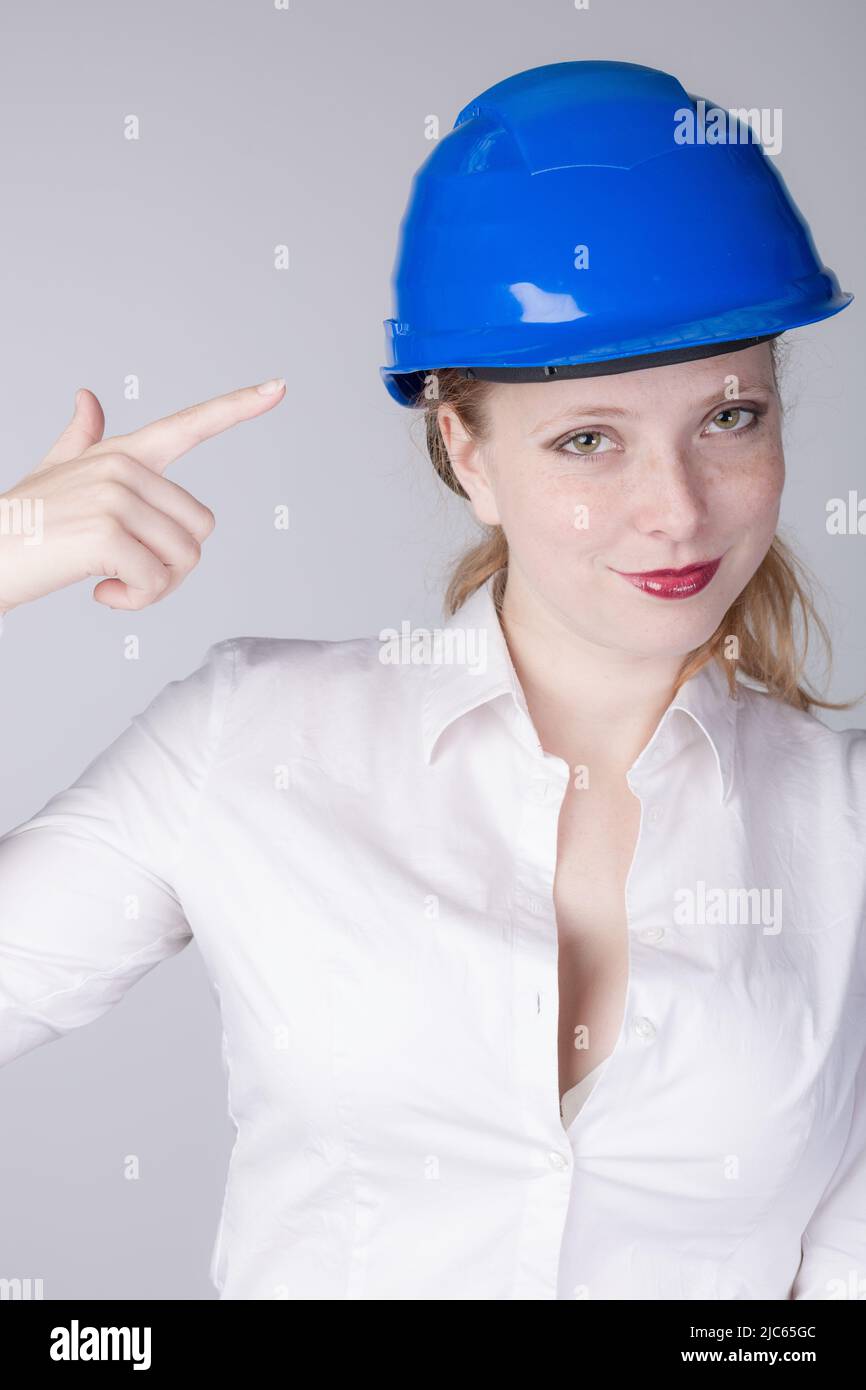 Young female engineer wearing a blue hard hat is pointing to it for ...