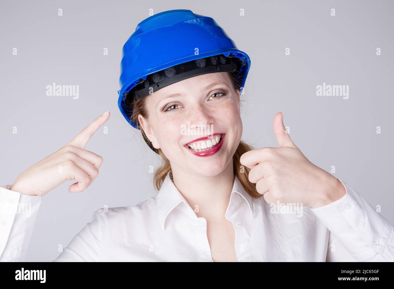 Young female engineer wearing a blue hard hat is making some gestures ...