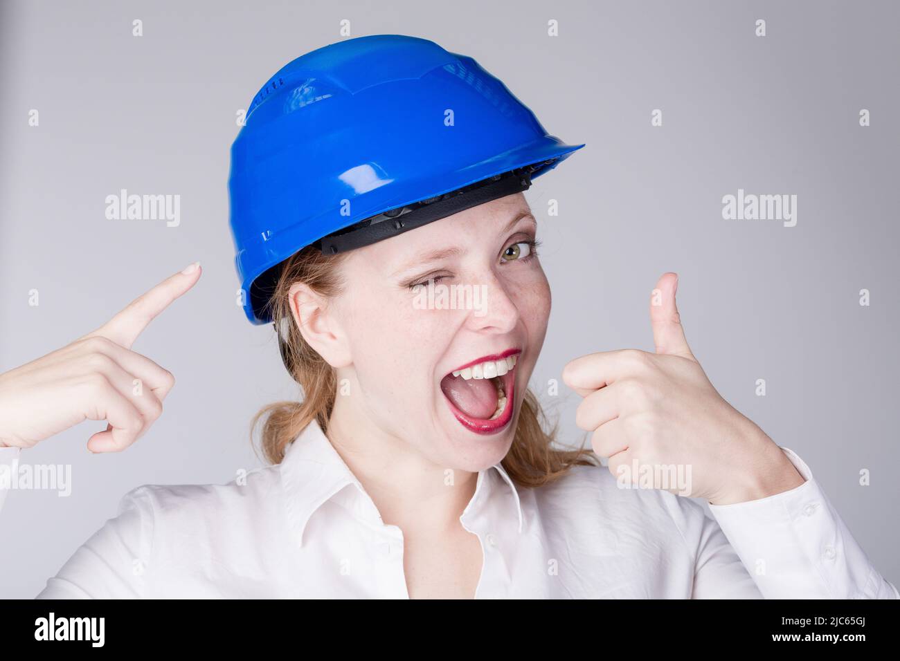 Young female engineer wearing a blue hard hat is making some gestures ...