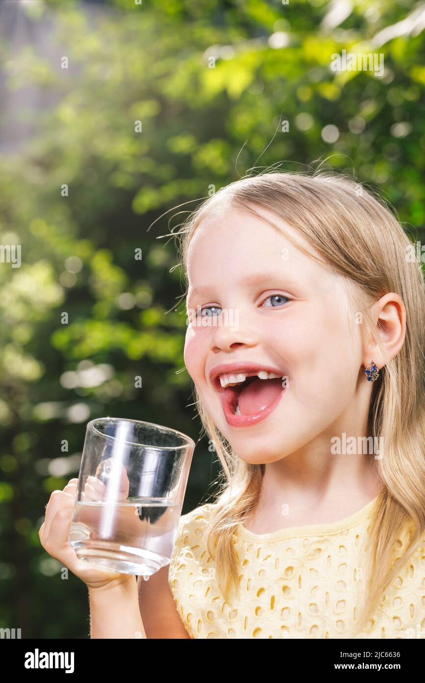 Happy little girl wearing yellow dress holding glass cup of water in a ...