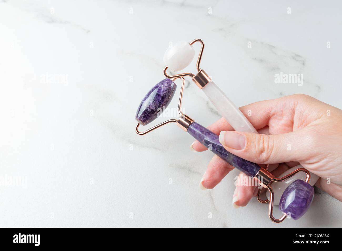 Female hand holding Rose quartz and amethyst face rollers for beauty ...