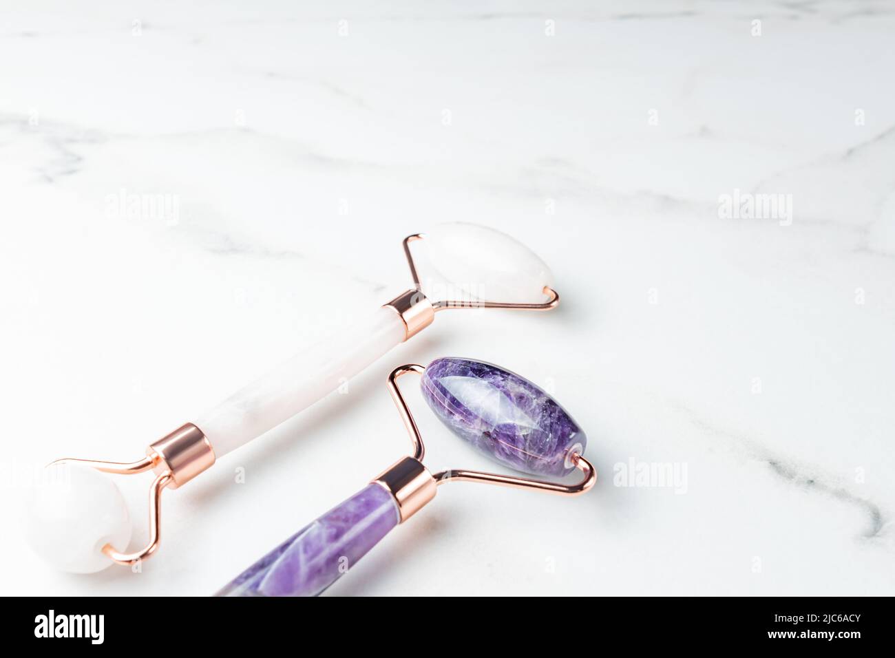 Rose quartz and amethyst face rollers on marble background, top view ...