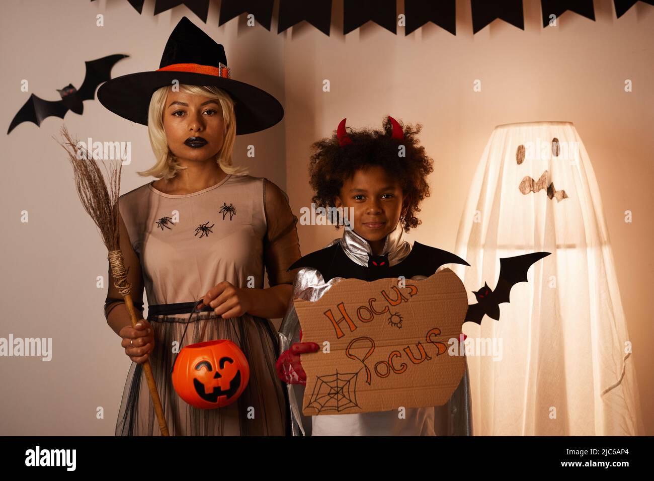 Portrait of serious young black mother in witchs dress and son in devil ...