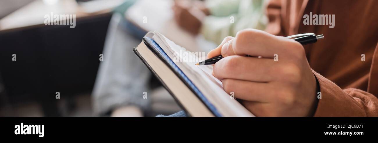 partial view of student writing in copybook on blurred background ...