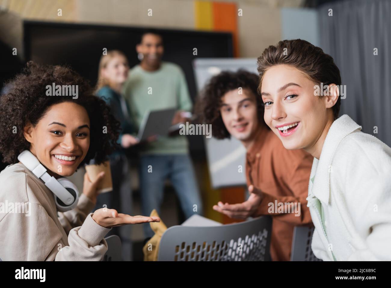 happy multiethnic students looking at camera near classmates on blurred ...