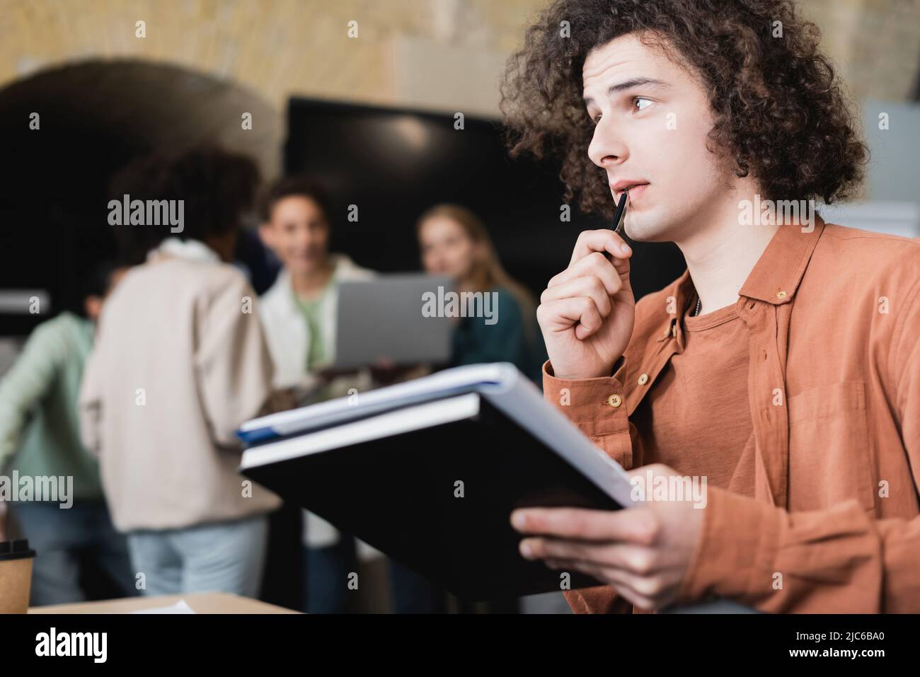 thoughtful student with copybooks looking away near classmates in ...