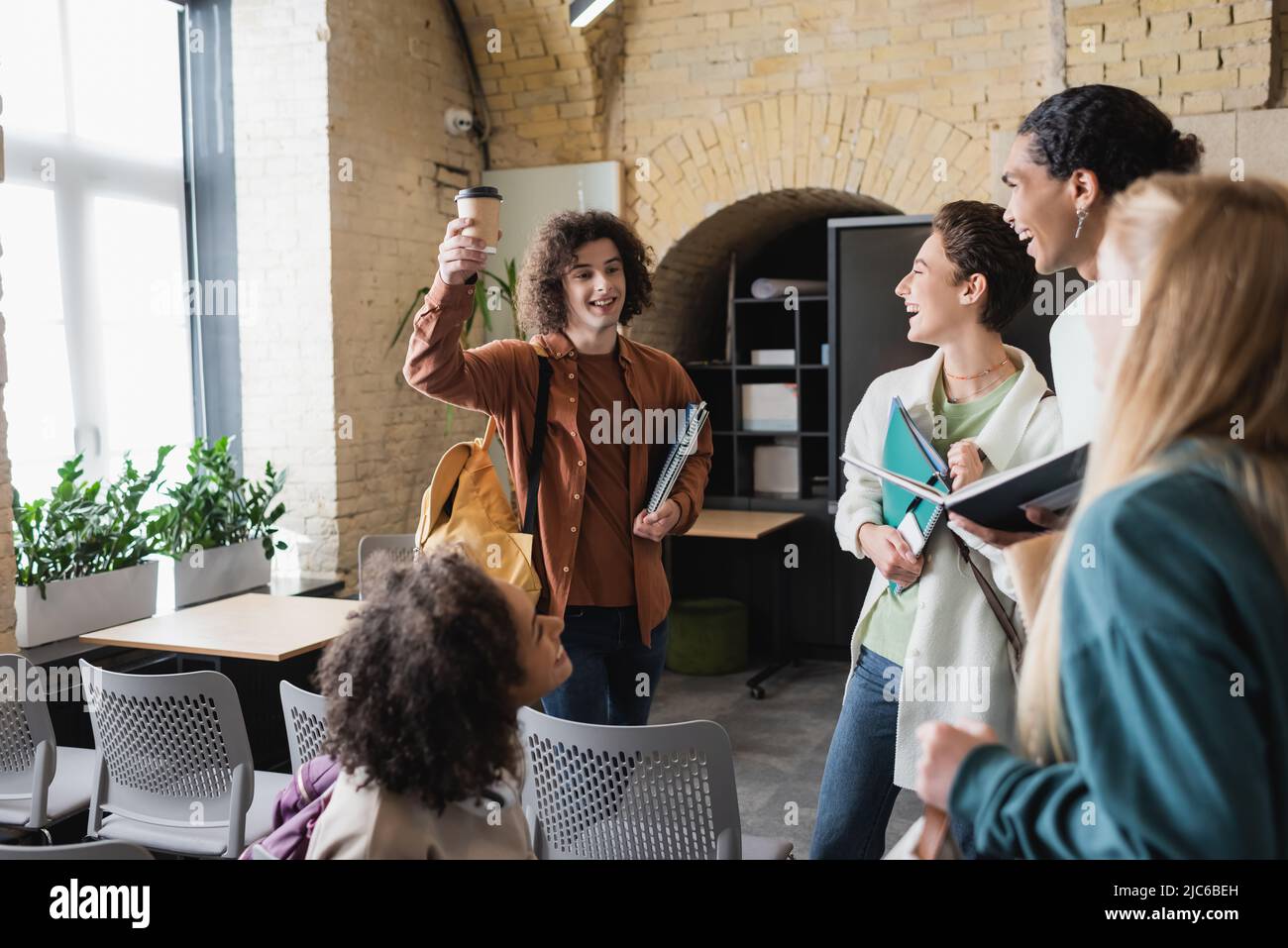 happy man toasting with paper cup near smiling multiethnic classmates ...