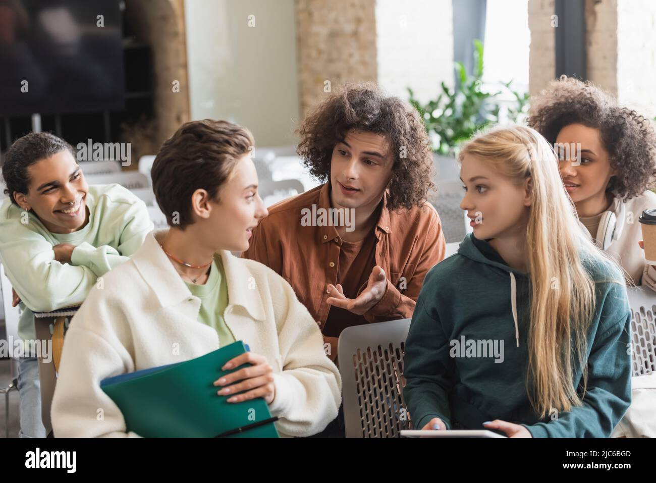 curly student pointing with hand while talking near multiethnic friends ...