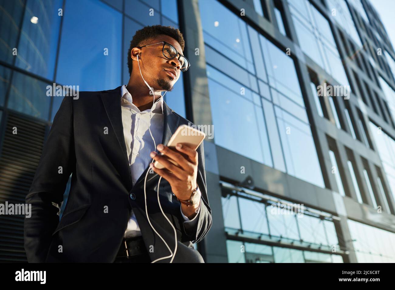 Below view of thoughtful young black businessman in earphone listening ...