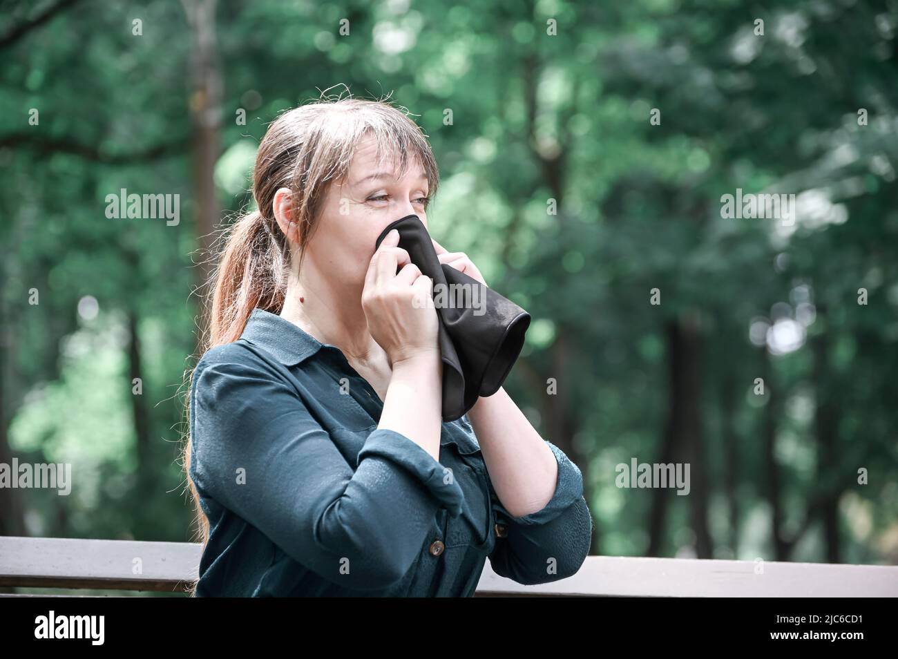 A woman blows her nose into a handkerchief while sitting on a bench in ...