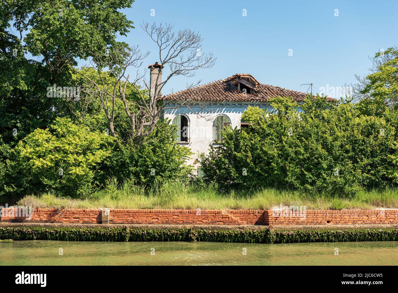 Abandoned and broken house in the Venice lagoon, partially hidden by ...