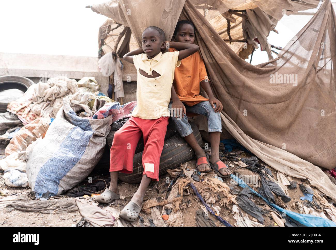 Two young desperate African children sitting on tires and waste on a ...