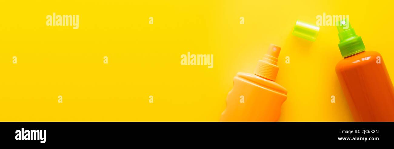 Top view of bottles of sunscreens near cap on yellow surface, banner ...