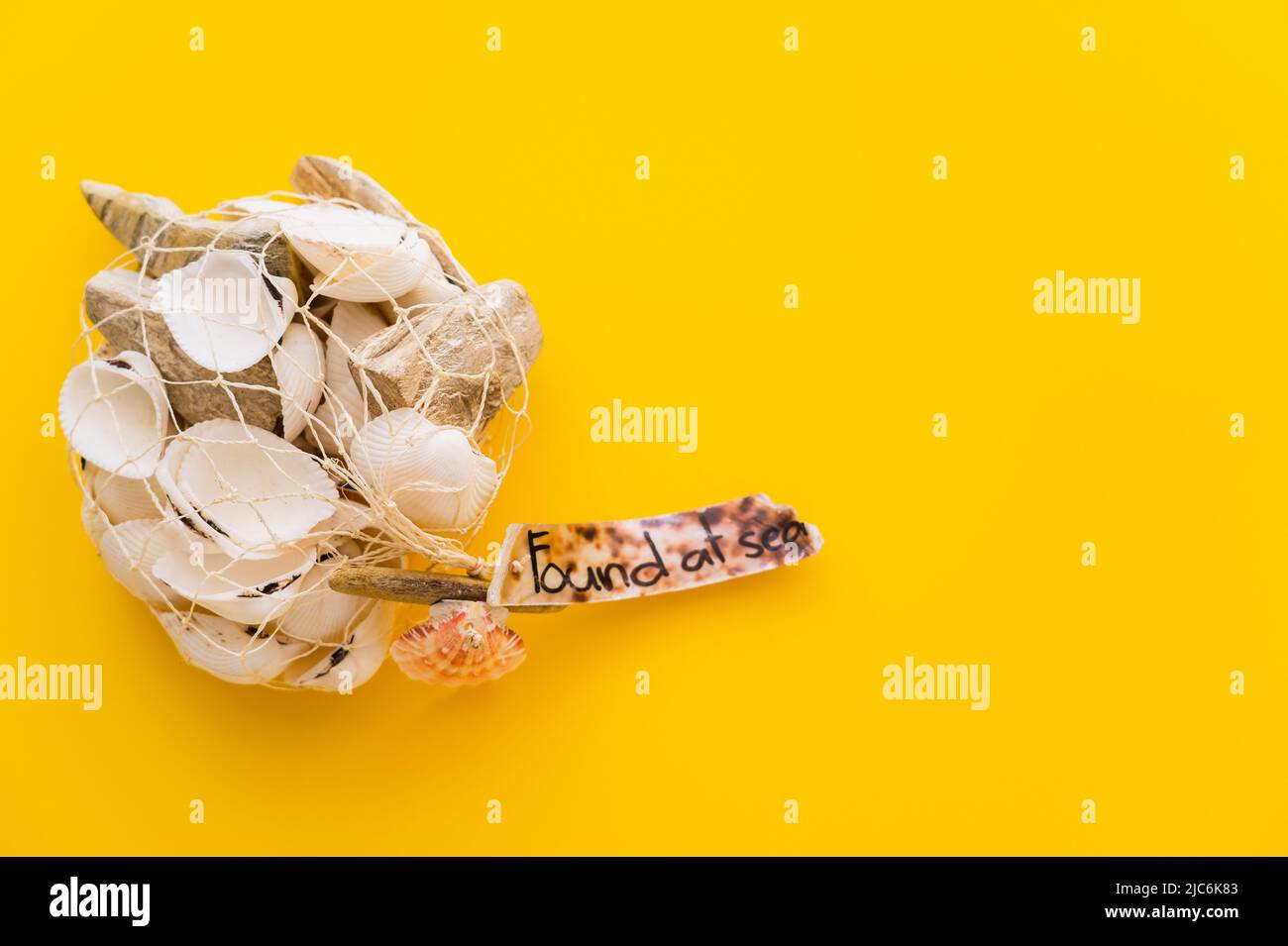 Top view of seashells in net with found at sea lettering on yellow ...