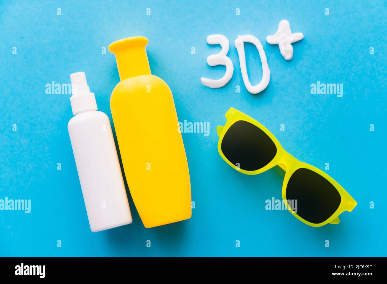Top view of sunscreens near 30+ signs and sunglasses on blue background ...