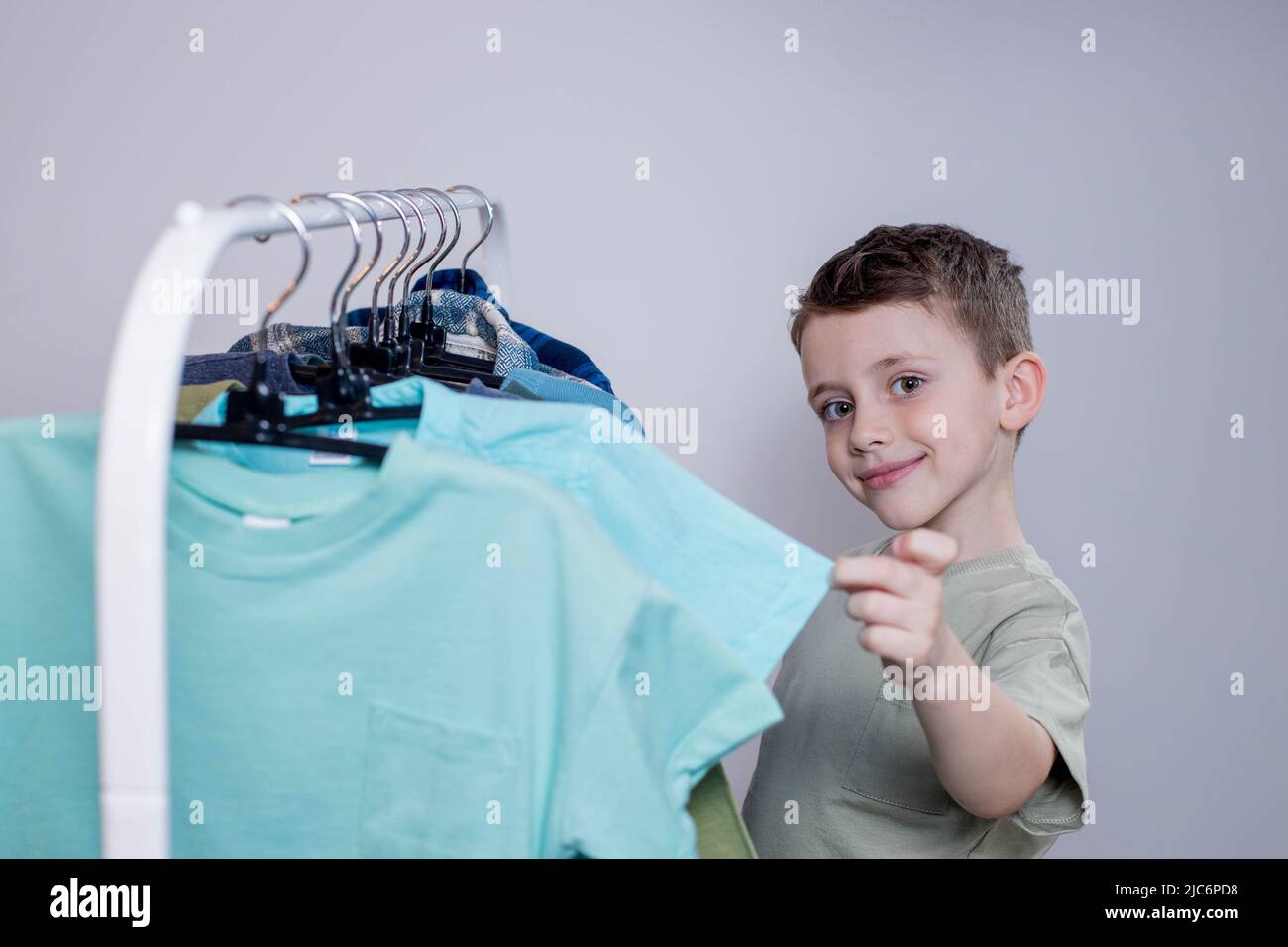 Boy preschooler standing by the hangers, racks up clothes, and chooses ...