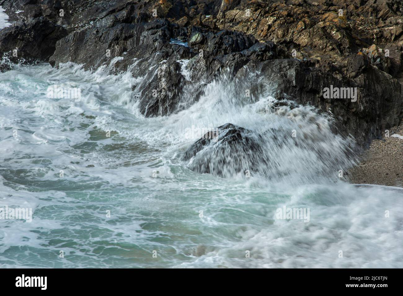 Incoming tide flowing swirling over jagged rocks in Fistral Bay in ...
