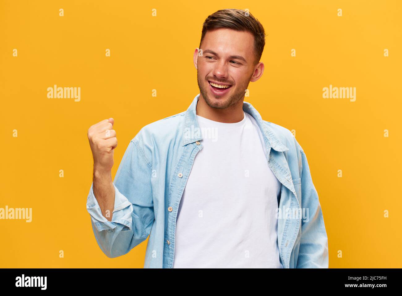 Lucky smiling tanned handsome man in blue basic t-shirt raise fist up ...