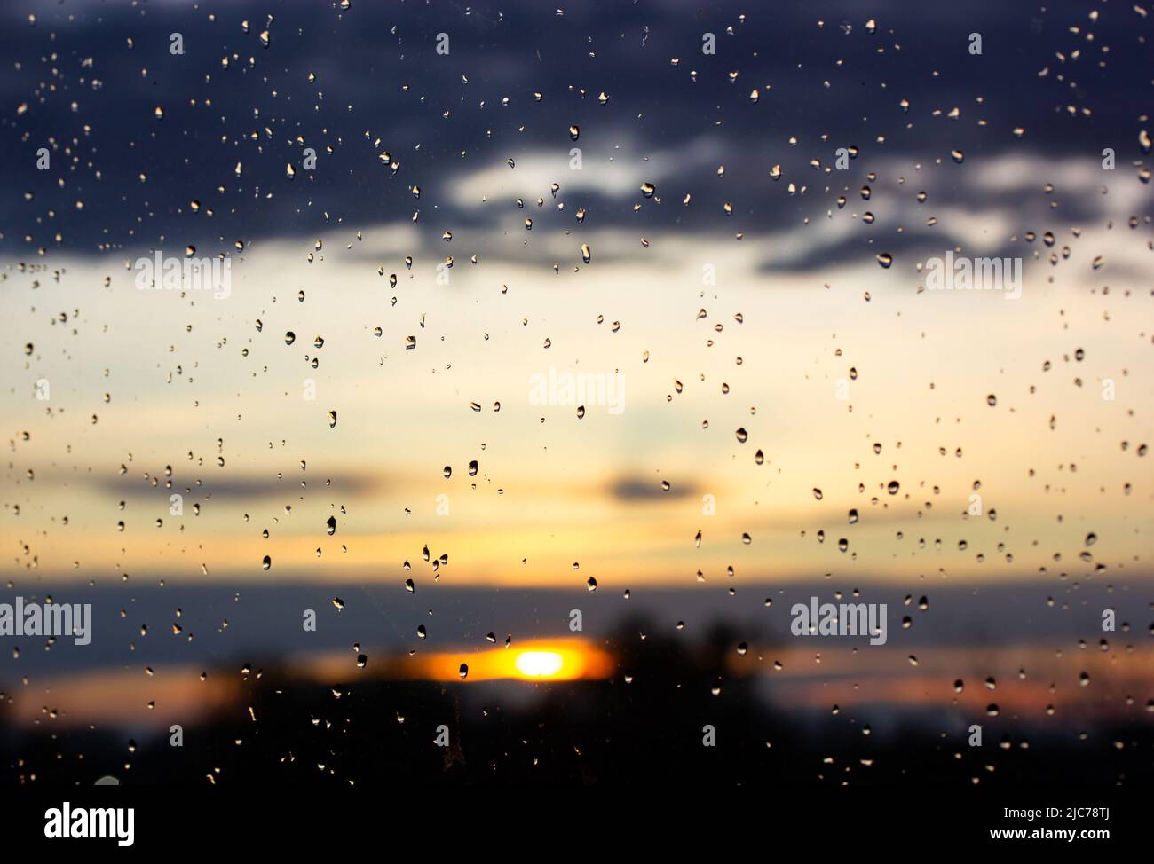 Rain at sunset. Wet window glass with raindrops against sun setting ...
