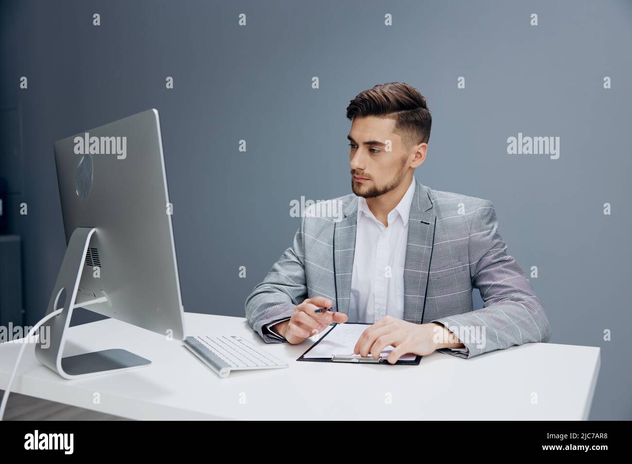 handsome man in a gray suit sits in front of a computer isolated ...