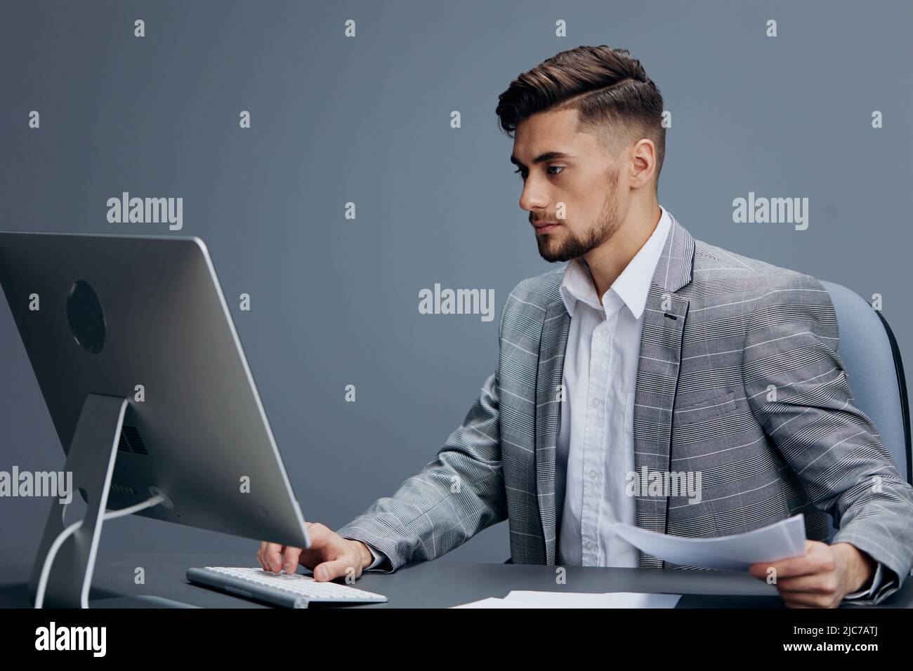 handsome man in a gray suit sits in front of a computer isolated ...